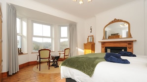 Quarto com cama grande, lareira, espelho e vista para o exterior pelas janelas.