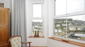 Quarto com janela panorâmica com vista para uma cidade, uma cadeira de madeira e um armário.