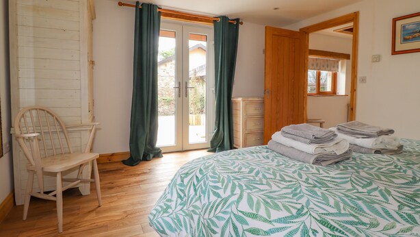 Quarto com cama, uma cadeira, cômoda e porta que dá para uma varanda.