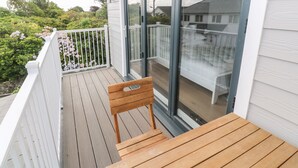 Um deck de madeira com um banco, uma porta de vidro que dá para uma varanda e um corrimão branco.