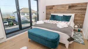 Quarto com uma janela grande, cama com roupa de cama verde-água, cabeceira de madeira e vista para o exterior.
