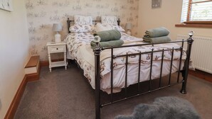 Quarto com cama, mesa de cabeceira e janela com persianas.
