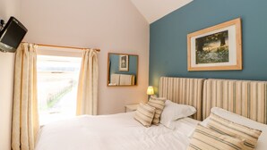 Quarto com cama, cortinas, televisão, quadro emoldurado e luminária.