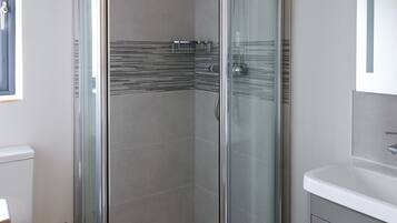 Um banheiro moderno com chuveiro em cabine de vidro, pia branca e piso revestido com azulejos.