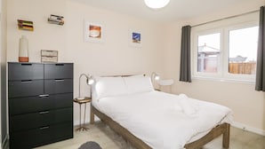 Quarto com cama, penteadeira, mesa de cabeceira, luminária e janela.