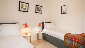 Quarto de hotel com duas camas, uma mesinha, duas luminárias e três quadros na parede.