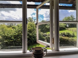 Uma janela com vista para uma paisagem verde, uma cerca de madeira e um objeto de metal no parapeito.