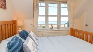 Quarto com cama, janela com vista para a praia e radiador sob a janela.