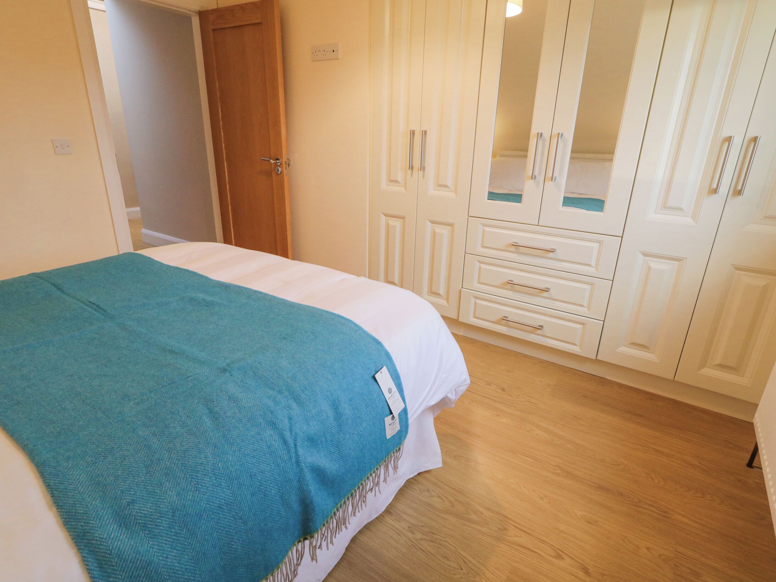 Quarto com cama, porta de madeira, armários brancos e piso de madeira.