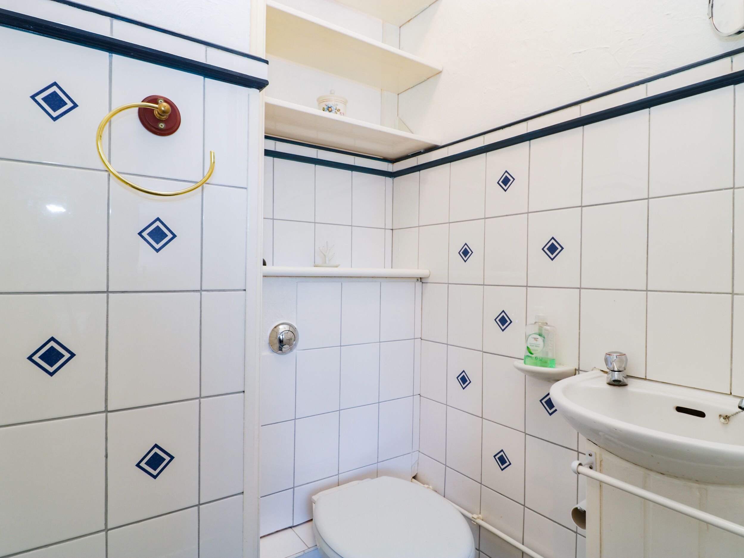 Casa de banho com azulejos brancos, sanita, lavatório e zona de duche.