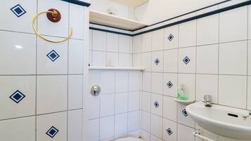 Casa de banho com azulejos brancos, sanita, lavatório e zona de duche.