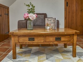 Uma mesa de centro de madeira com duas gavetas, um vaso com flores e uma placa com a inscrição 'Guest Book'.