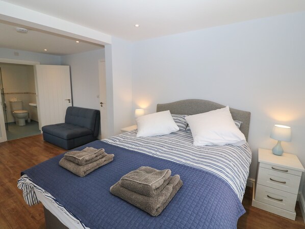 Quarto com uma cama, duas mesinhas de cabeceira, uma cadeira e banheiro visível por uma porta aberta.