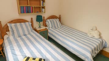 Quarto com duas camas de solteiro, mesa de cabeceira com abajur, estante de livros e um ursinho de pelúcia em uma das camas.