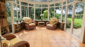 Uma estufa com cadeiras de vime, uma mesa e vista para o jardim.