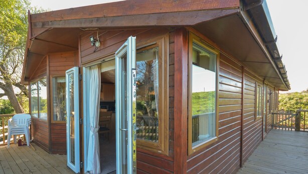 Uma cabana de madeira com varanda, janelas amplas e porta deslizante.