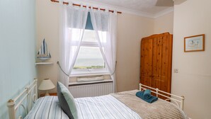 Quarto com cama, janela com vista, guarda-roupa de madeira e uma pequena estante com uma réplica de um veleiro.