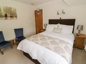 Quarto com cama grande, duas mesas de cabeceira, uma cadeira e uma porta com sinal de emergência.
