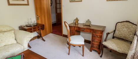 Quarto com escrivaninha de madeira, duas cadeiras, um sofá, mesa de centro com jogo de Scrabble e quadros nas paredes.