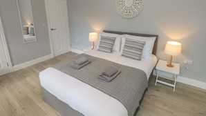 Quarto bem arrumado com uma cama grande, duas mesas de cabeceira, um espelho e um objeto decorativo na parede.