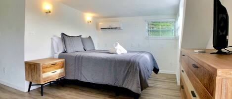 Quarto com cama, cómoda de madeira e televisão sobre um móvel de madeira.