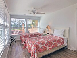 Quarto com duas camas, um ventilador de teto, janela com persianas e vista para o exterior.