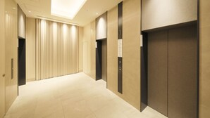 Um corredor moderno com elevadores, uma luminária no teto e um piso com padrão em azulejos claros.