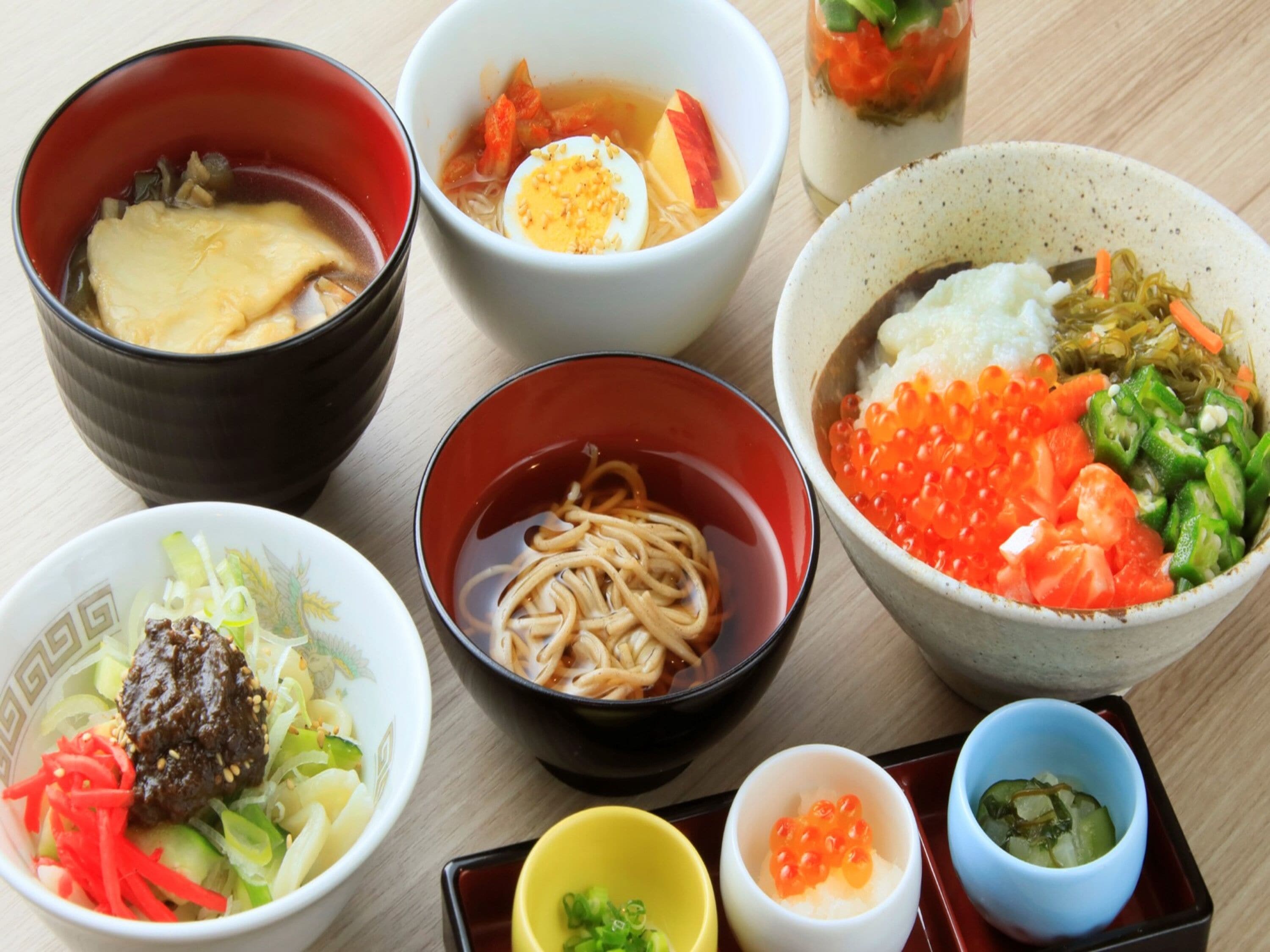 Diversos recipientes com diferentes tipos de pratos japoneses, incluindo macarrão, sopa e frutos do mar.