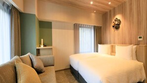 Quarto de hotel com uma cama grande, um sofá, mesa de cabeceira e luminária fixa na parede.