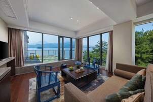 Uma sala de estar moderna com uma janela ampla, uma televisão de tela plana, um sofá, uma mesa de centro e uma poltrona.