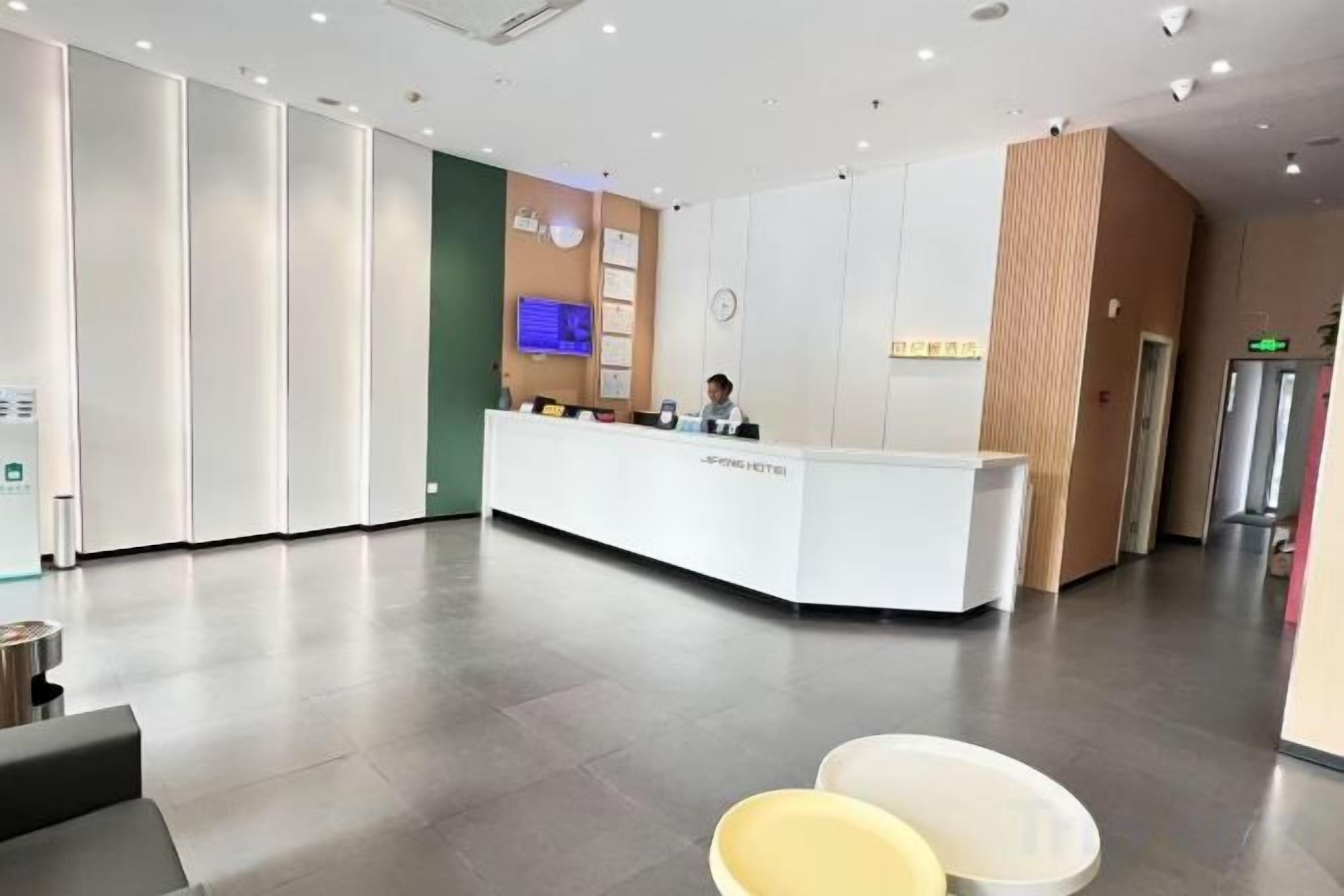 Uma área de recepção de hotel, com balcão, relógio e tela digital.