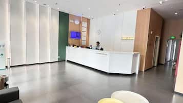 Uma área de recepção de hotel, com balcão, relógio e tela digital.