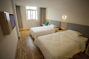 Quarto de hotel com duas camas, uma janela com cortinas, uma mesa de cabeceira com abajur e uma TV fixada na parede.