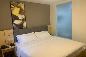Quarto de hotel com cama, mesa de cabeceira, obra de arte na parede e uma porta.