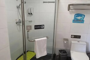 Uma casa de banho pequena com cabine de chuveiro em vidro, sanita branca e um contentor de lixo.