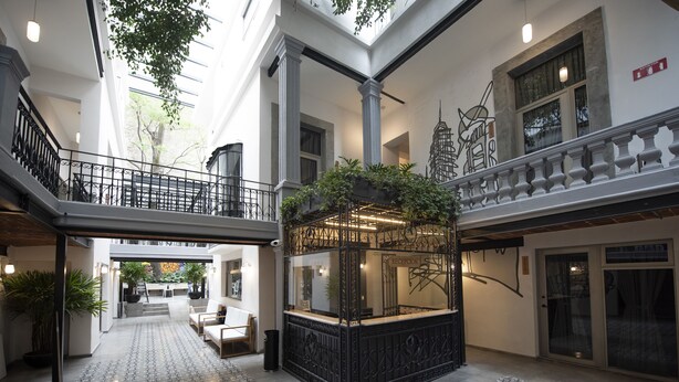 Um átrio espaçoso com uma área de recepção central, uma escadaria e uma varanda com guarda-corpo.
