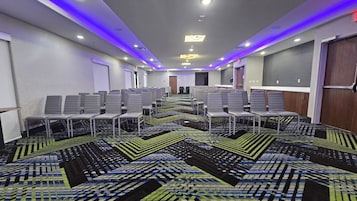 Uma sala de conferências com fileiras de cadeiras, carpete estampado e iluminação embutida no teto.