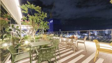 Um terraço no telhado com mesas ao ar livre, vista para a cidade e um edifício ao fundo.