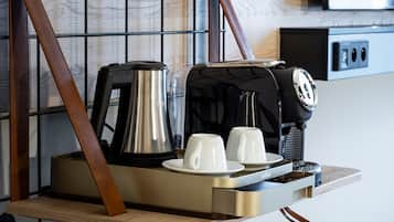 Uma cozinha compacta com cafeteira, duas xícaras brancas e chaleira em bancada de madeira.
