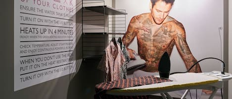 Pessoa a passar roupa numa tábua de passar com um guia na parede.