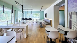 Um restaurante moderno com um balcão comprido, várias mesas e cadeiras. Janelas amplas oferecem luz natural e vista para o exterior.