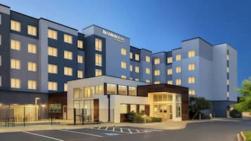 Hotel de vários andares com fachada moderna, entrada imponente e estacionamento com acessibilidade para pessoas com deficiência.