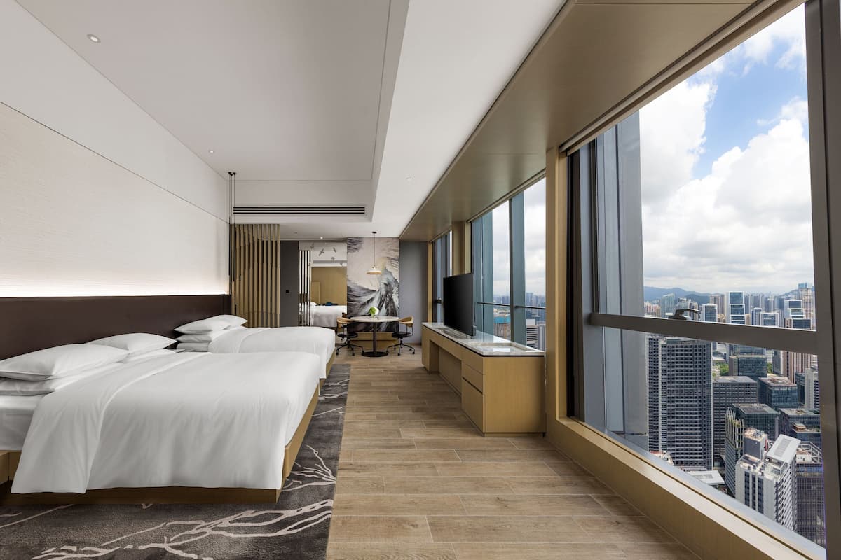 Quarto de hotel moderno com uma cama grande, uma escrivaninha e vista para a cidade.