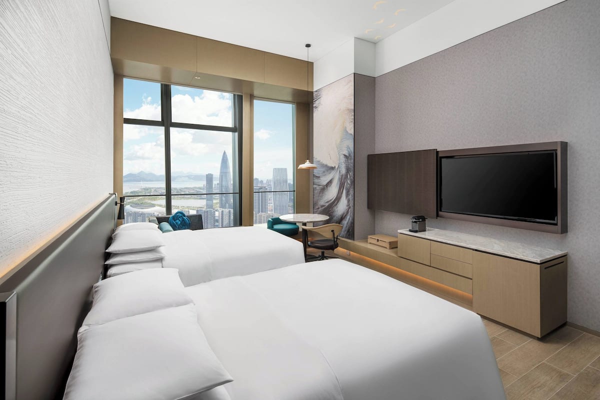 Quarto de hotel com duas camas, televisão, escrivaninha e vista para a cidade.
