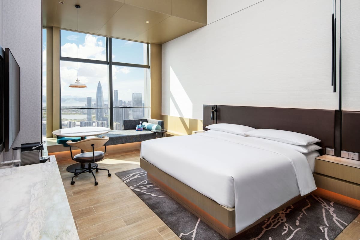Quarto de hotel moderno com uma cama grande, uma escrivaninha e vista para o horizonte da cidade.