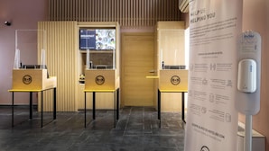 Uma área de recepção de hotel com um balcão de madeira, um ecrã digital a mostrar opções de pequeno-almoço e um cartaz com as regras do hotel.