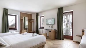 Quarto de hotel com duas camas, uma escrivaninha, televisão e vista para árvores.