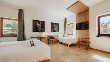 Quarto de hotel com duas camas, uma escrivaninha, uma cadeira, televisão e obras de arte nas paredes.