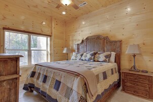 Quarto de cabana de madeira com uma cama grande, duas mesas de cabeceira com abajures e uma janela com persianas.