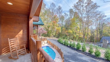 Uma cabana de madeira com piscina, cadeira de balanço e vista para uma floresta.